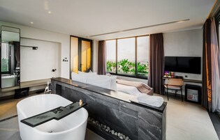 Quarto de hotel moderno com uma banheira grande, televisão de tela plana e vista para a cidade através de amplas janelas.