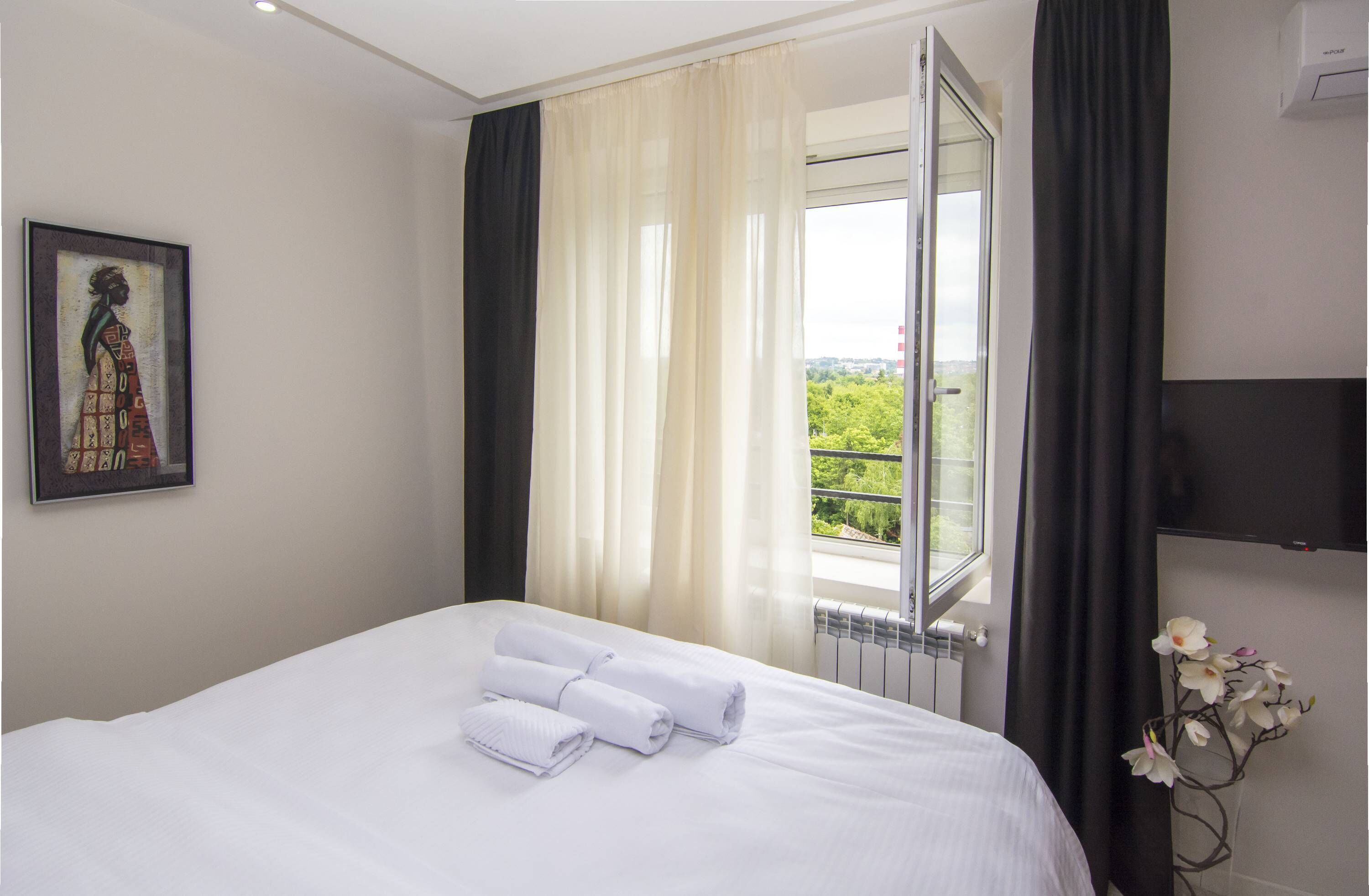 Quarto de hotel com cama, janela com cortinas, radiador e um quadro na parede.