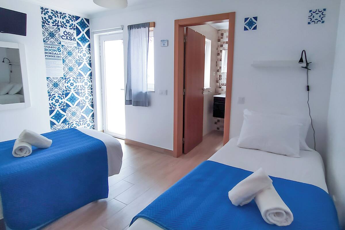 Quarto de hotel com duas camas, banheiro e vista para a rua.