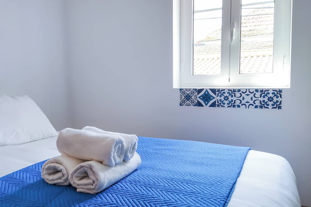 Cama bem arrumada com um edredom azul, travesseiros brancos e uma toalha dobrada em cima.