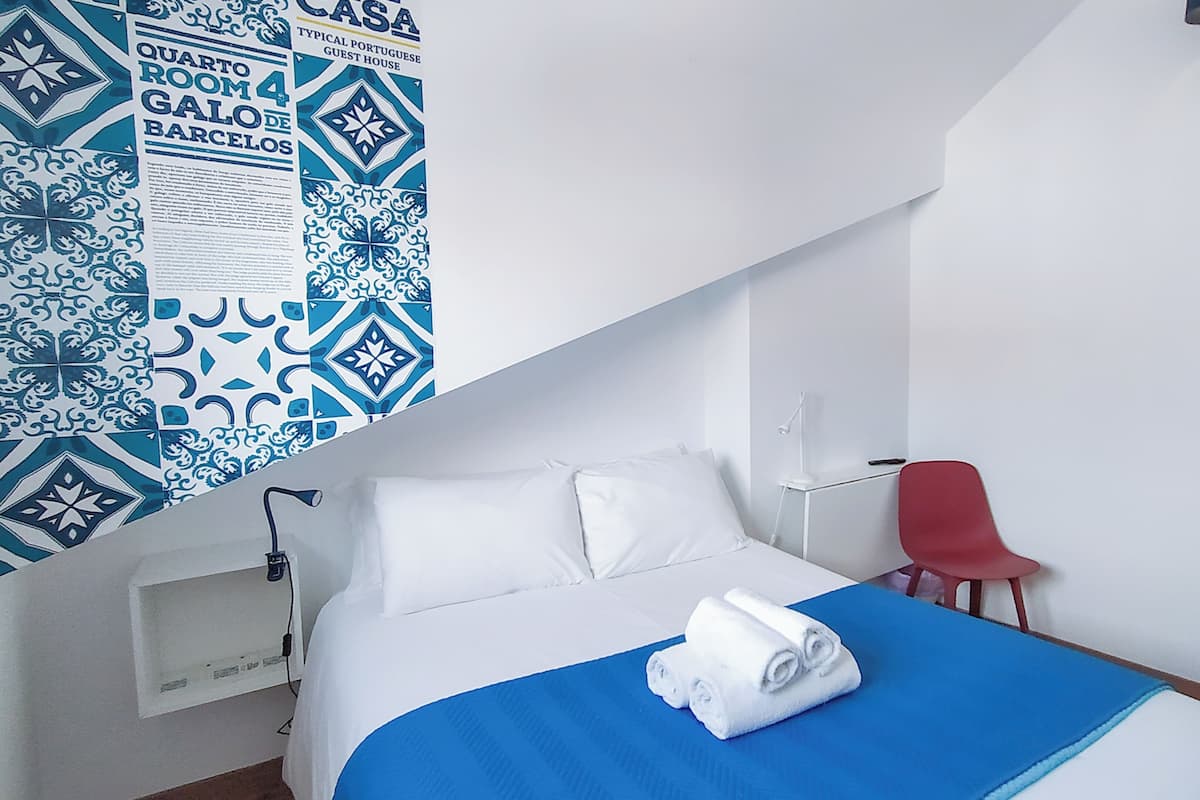 Quarto com cama, cadeira vermelha, manta azul e parede estampada.