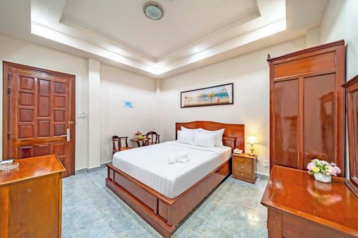 Quarto de hotel com cama grande, guarda-roupa de madeira, escrivaninha e um quadro na parede.