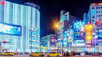 Rua urbana iluminada à noite, com painéis luminosos e letreiros de neon, incluindo uma loja H&M em destaque.