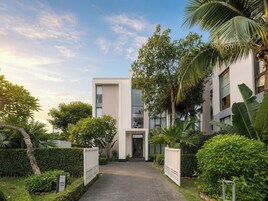 Um edifício moderno com entrada central, rodeado por vegetação exuberante e palmeiras.