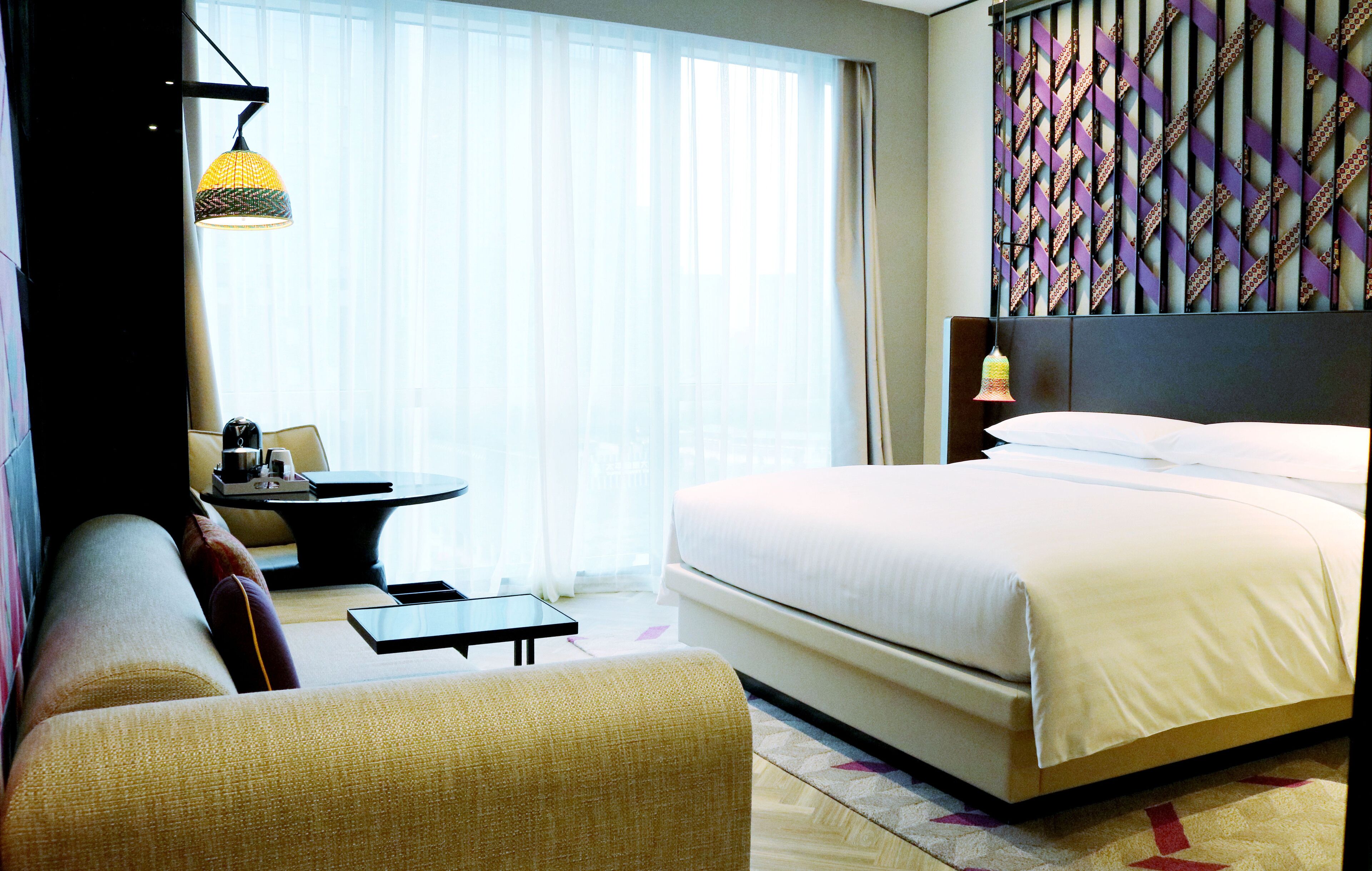 Quarto de hotel com uma cama grande, um sofá, uma mesinha e uma luminária.