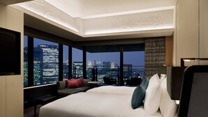 Quarto de hotel moderno com uma cama grande, um sofá, uma escrivaninha e vista para o horizonte da cidade.