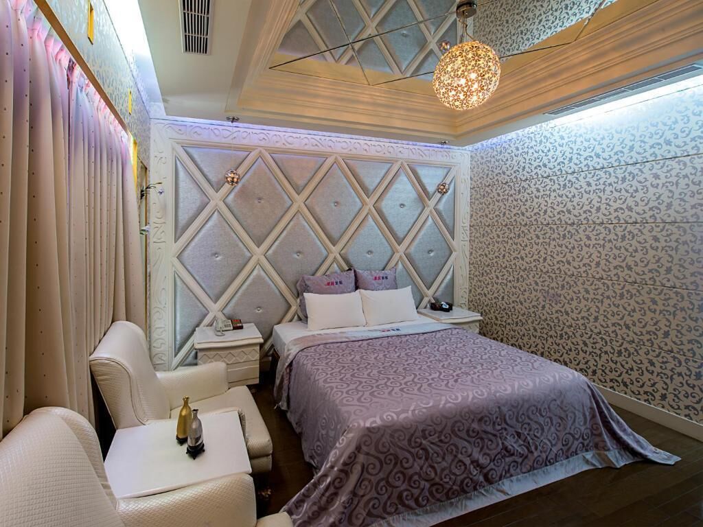 Quarto com cama, mesa de cabeceira, cadeira e luminária decorativa no teto.