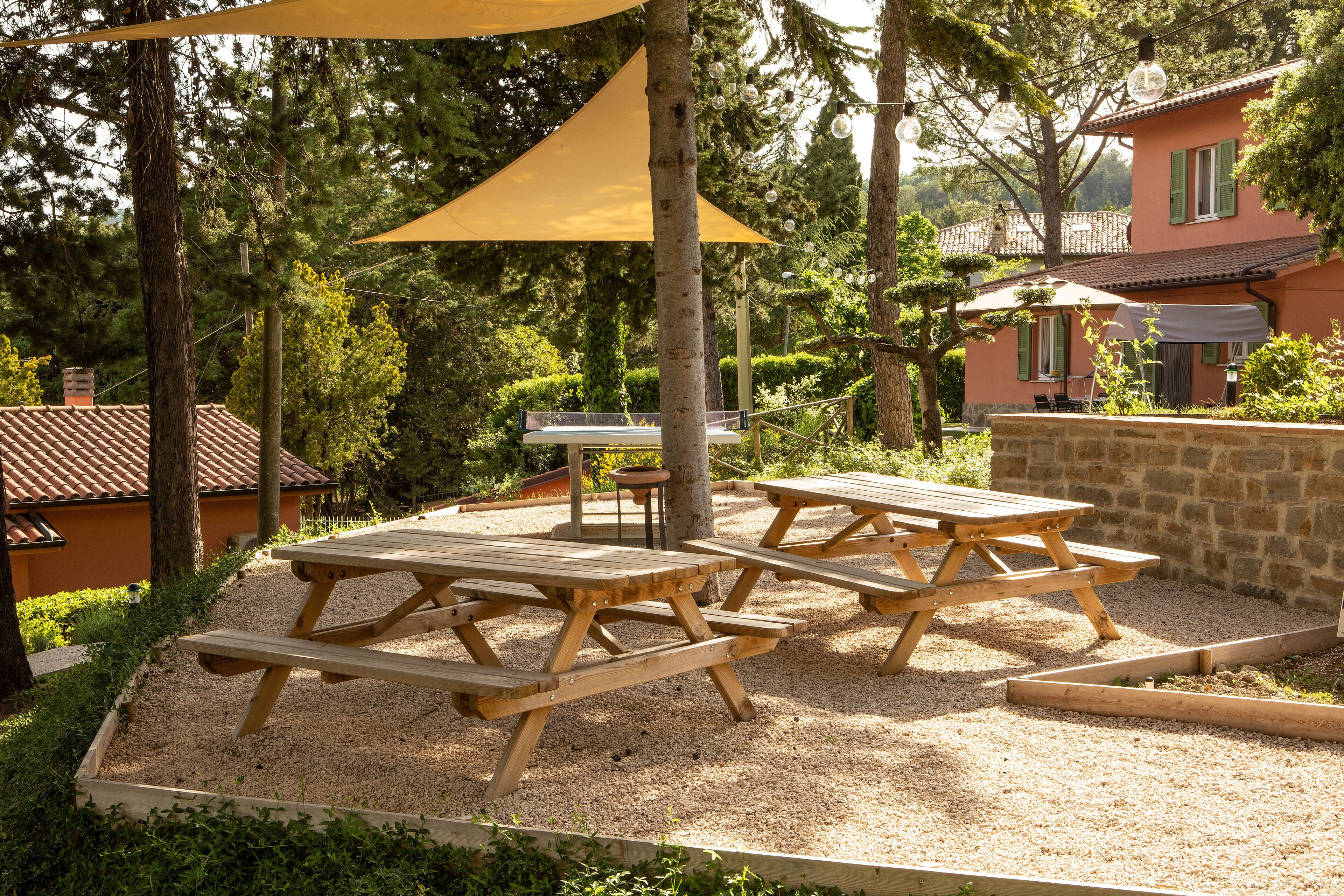 Área de pátio externo com mesas de piquenique e um guarda-sol amarelo.