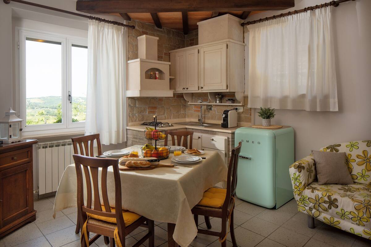 Uma área de refeições com uma mesa posta para o café da manhã, uma geladeira antiga e vista para o exterior.