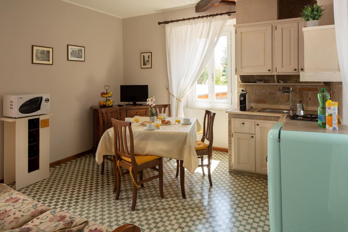 Uma área de refeições com uma mesa posta para dois, micro-ondas, televisão e uma janela com cortinas.