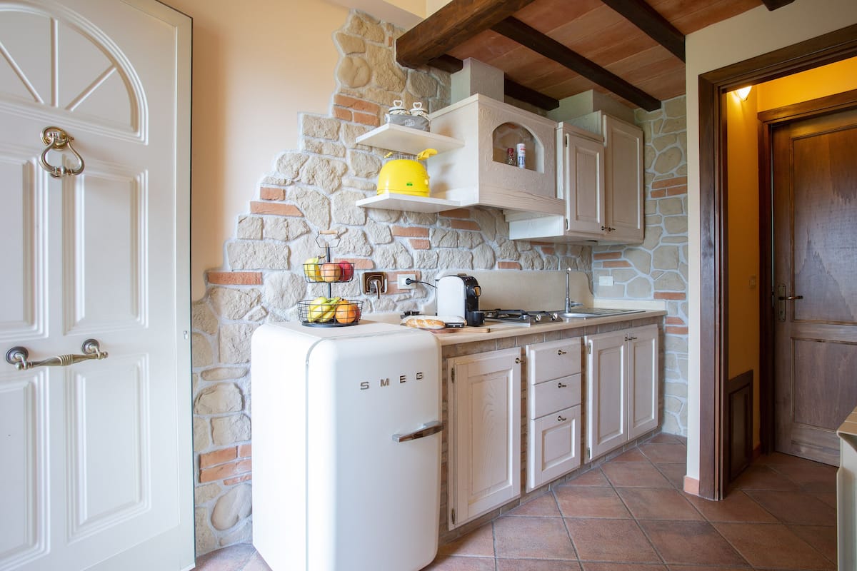 Uma cozinha com geladeira branca, armários de madeira e parede de pedra.