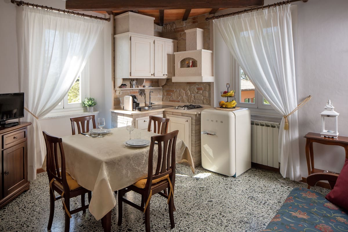 Uma cozinha compacta com mesa, cadeiras, geladeira e janela com cortinas.