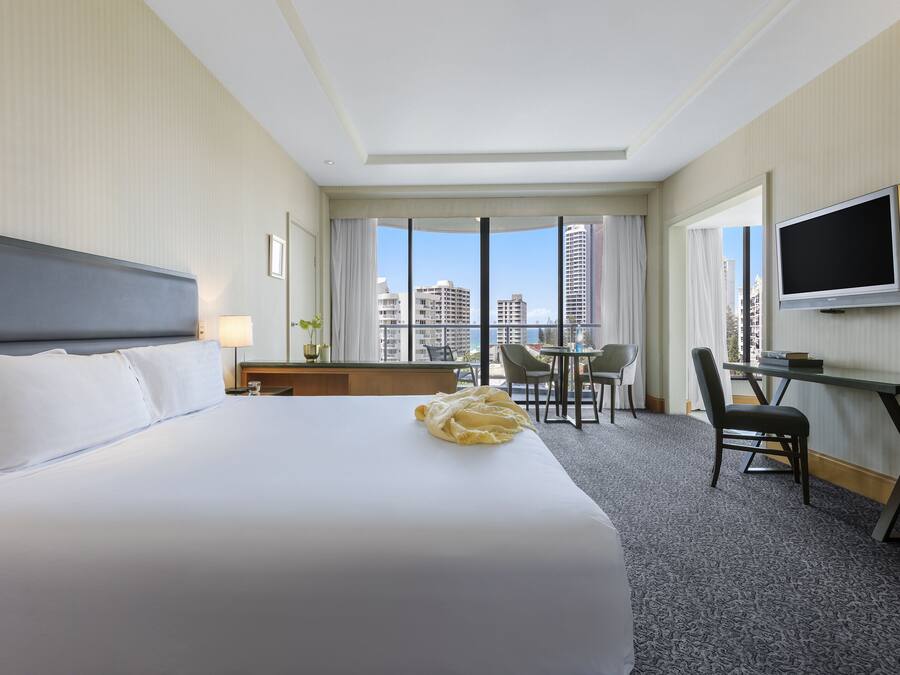 Quarto de hotel com uma cama grande, uma escrivaninha, uma cadeira, uma televisão e vista para a cidade.