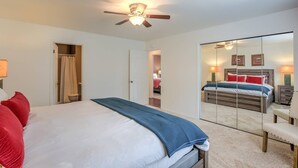 Um quarto com uma cama, ventilador de teto, espelho e porta que dá para outro cômodo.