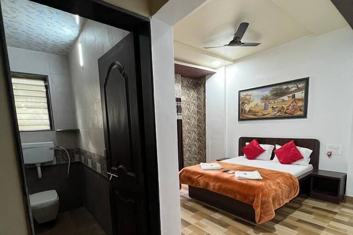 Quarto com cama, mesa de cabeceira, pintura na parede e banheiro com vaso sanitário e pia.