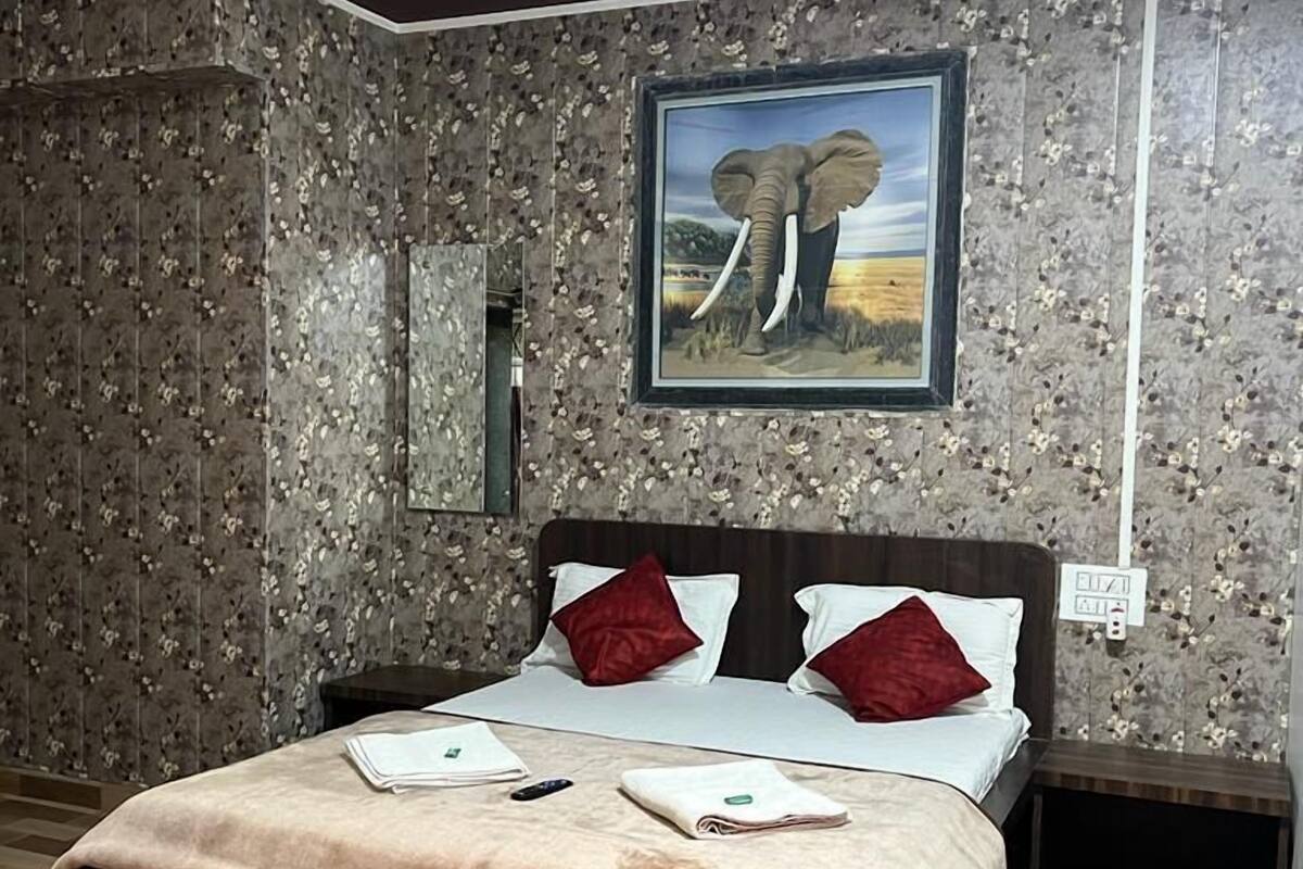 Quarto com cama, mesa de cabeceira, ventoinha no teto e espelho fixado na parede.