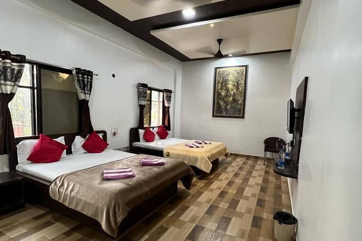 Quarto de hotel com duas camas, um ventilador de teto, um quadro e uma televisão na parede.