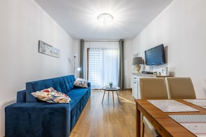 Uma sala de estar moderna com um sofá azul, uma mesa de jantar de madeira e uma televisão.