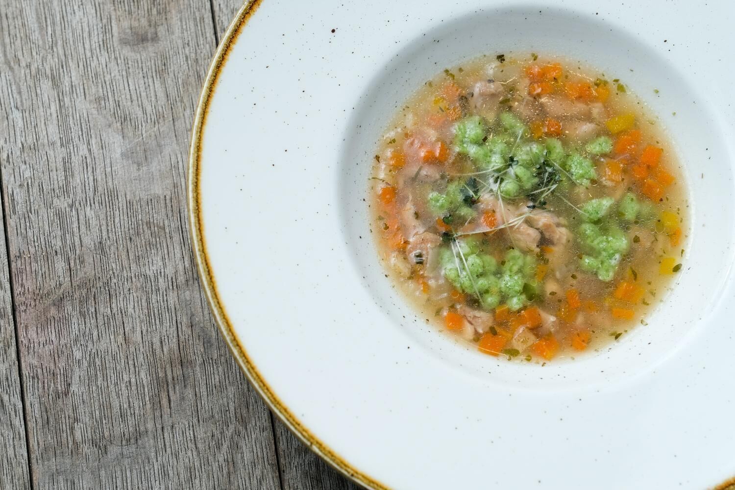 Uma tigela de sopa com legumes e ervas sobre uma mesa de madeira.