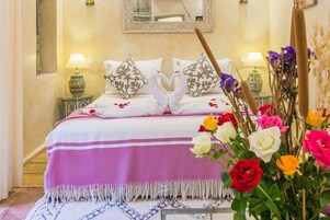 Quarto de hotel com cama, almofadas decorativas, abajur, espelho e um vaso de flores.