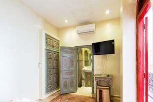 Um corredor com portas ornamentadas, uma TV montada e piso de azulejos.