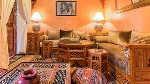 Quarto tradicional marroquino com um sofá, almofadas estampadas, uma mesa de centro de madeira e uma luminária decorativa.