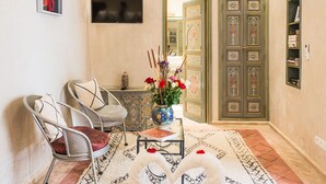 Quarto com duas cadeiras de metal, um tapete estampado, um vaso com flores e uma porta tradicional com desenhos detalhados.