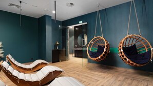 Um spa moderno com piso de madeira, uma mesa de massagem e duas cadeiras de ratã suspensas.