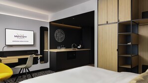 Quarto de hotel com cama, escrivaninha, cadeira, pequeno kitchenette e guarda-roupa.