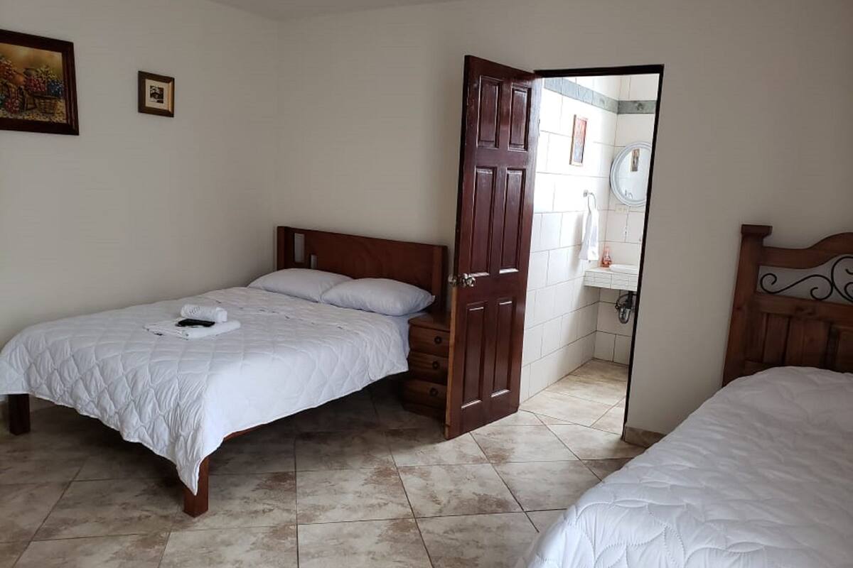 Quarto com cama, porta de madeira, banheiro com espelho e chão em azulejo.