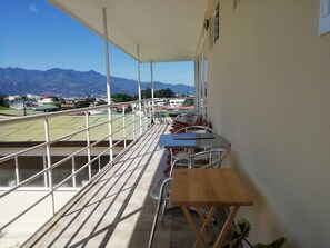 Varanda com vista para montanhas, chão de azulejos e cadeiras e mesas de metal.