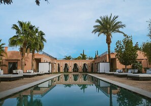 Área de piscina com espreguiçadeiras, palmeiras e um edifício com arcos.