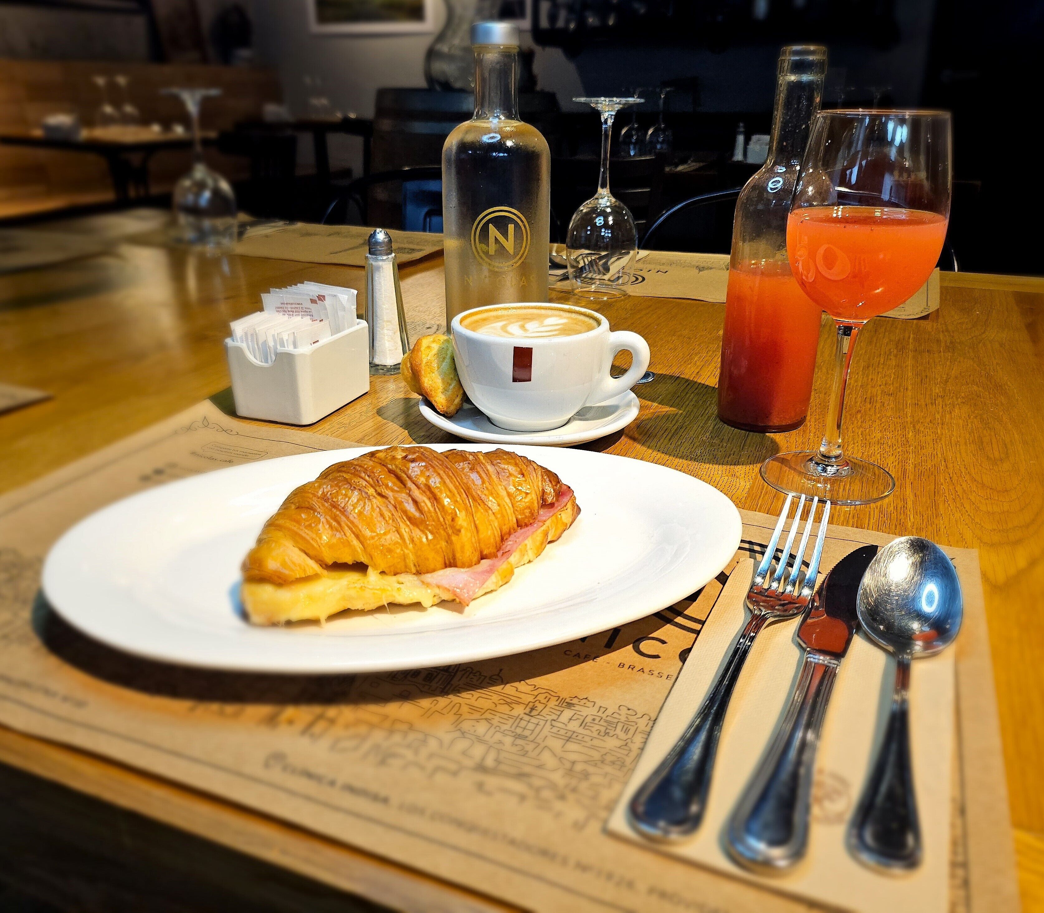 Um ambiente de café da manhã com um croissant, café e um copo de suco sobre uma mesa de madeira.