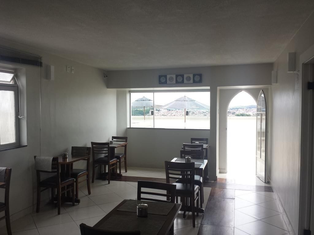 Uma sala de jantar com mesas e cadeiras, grandes janelas com vista para uma montanha e paisagem urbana, e uma porta que dá para o exterior.