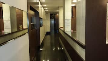 Corredor com pisos refletivos, lambris de madeira e portas de vidro que dão acesso a quartos.