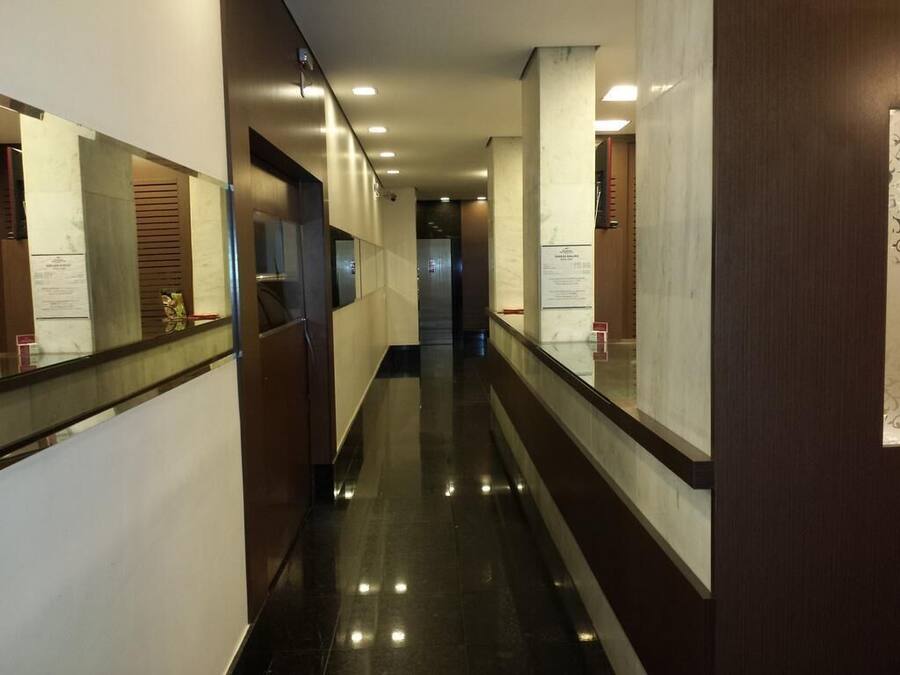 Corredor com pisos refletivos, lambris de madeira e portas de vidro que dão acesso a quartos.