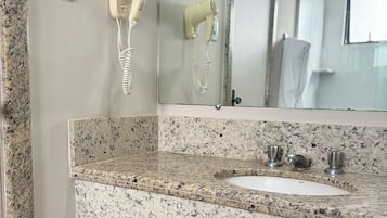 Casa de banho com bancada de granito, lavatório e secador de cabelo fixado na parede.