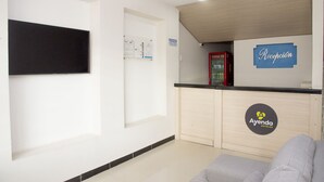 Uma área de recepção de hotel com uma televisão de tela plana, um balcão de atendimento e uma placa indicando a recepção.