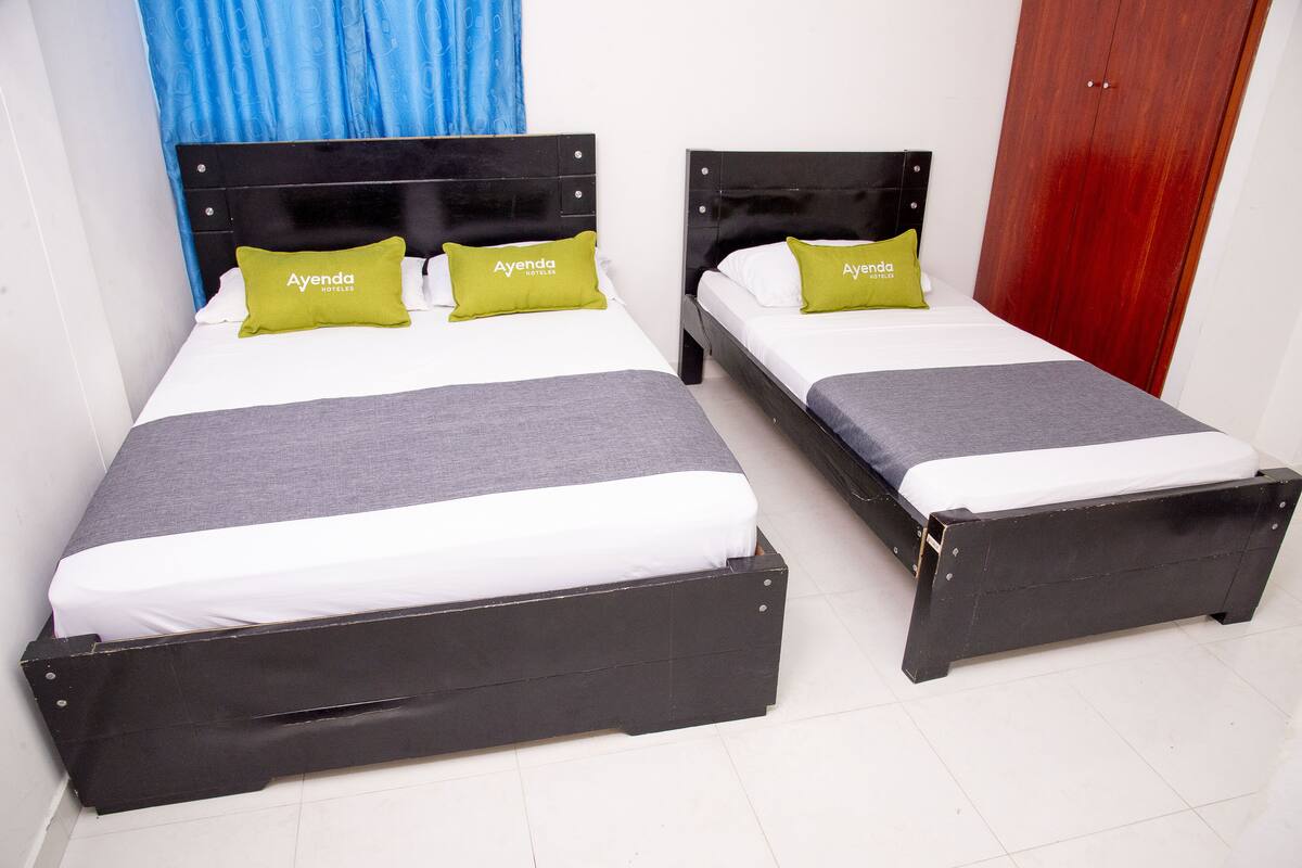 Duas camas de solteiro com estrutura preta e roupa de cama branca, cada uma com almofada verde identificada com a etiqueta "Ayenda Hotels".