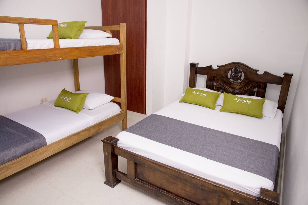 Duas camas beliche com estrutura de madeira e roupa de cama branca, cada uma com almofada verde com a etiqueta "Ayenda Hotels".