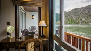 Quarto com uma escrivaninha, cadeiras, abajur, globo e vista para um lago e montanhas.