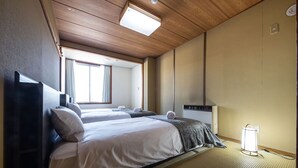 Quarto de hotel com duas camas, ventilador de teto, aquecedor e janela com cortinas.