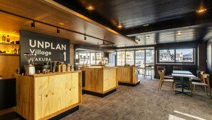 Um espaço de bar moderno com balcões e assentos de madeira, amplas janelas com vista para a cidade e uma placa chamativa com a inscrição "UNPLAN Village 1".