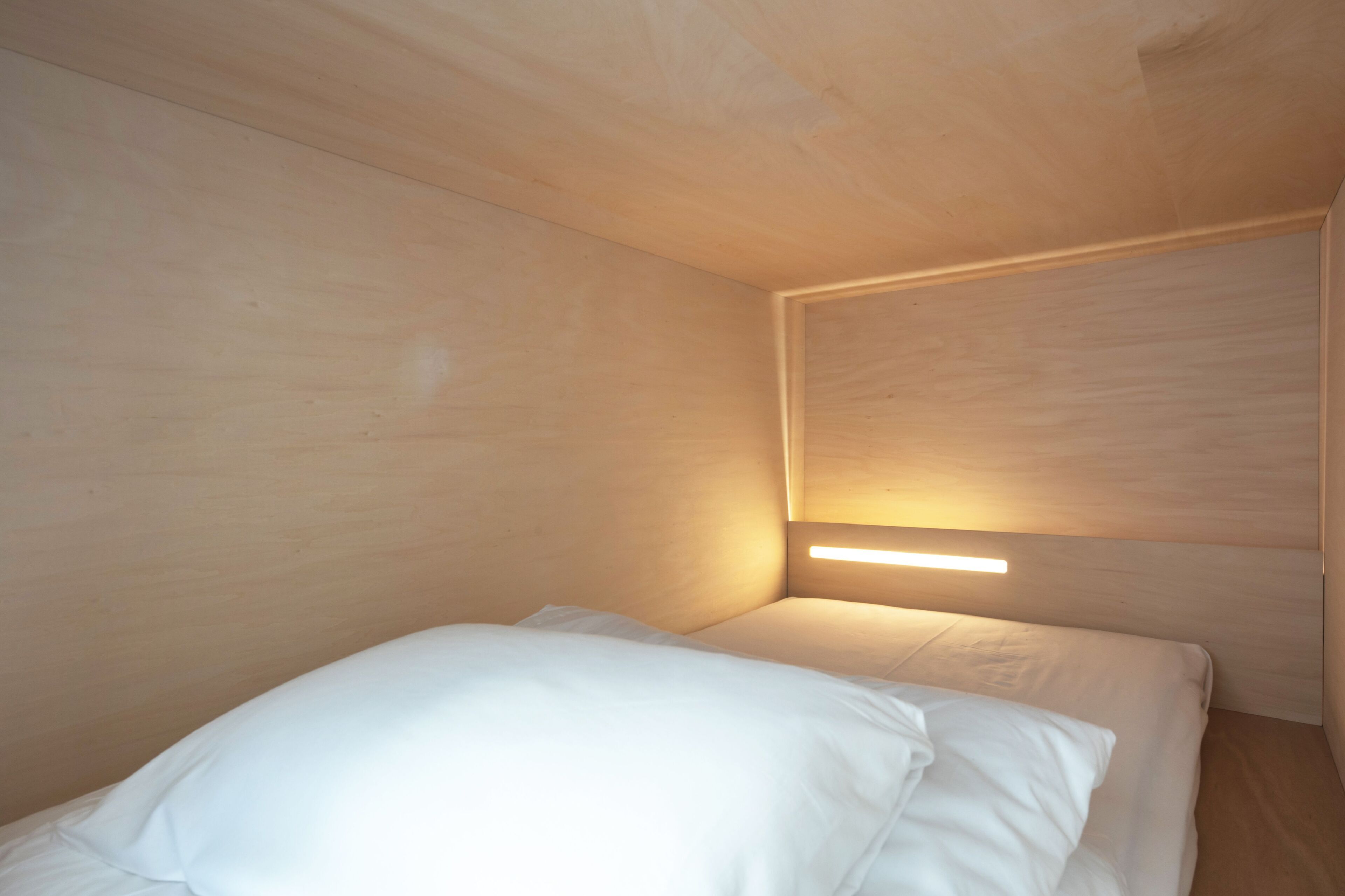 Quarto pequeno com cama de solteiro, cabeceira de madeira e mesa de cabeceira.