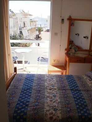 Quarto com cama, uma mesinha, uma cadeira e vista para a varanda externa.