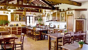 Uma cozinha rústica com vigas de madeira, um espaço de refeições com mesas e cadeiras de madeira, além de utensílios de cozinha e plantas.