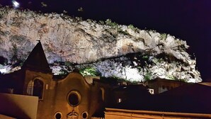 Um edifício com uma torre imponente e uma grande formação rochosa iluminada ao fundo.