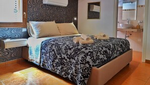 Um quarto com cama, mesa de cabeceira, ar condicionado, espelho e banheiro com pia e porta-toalhas.