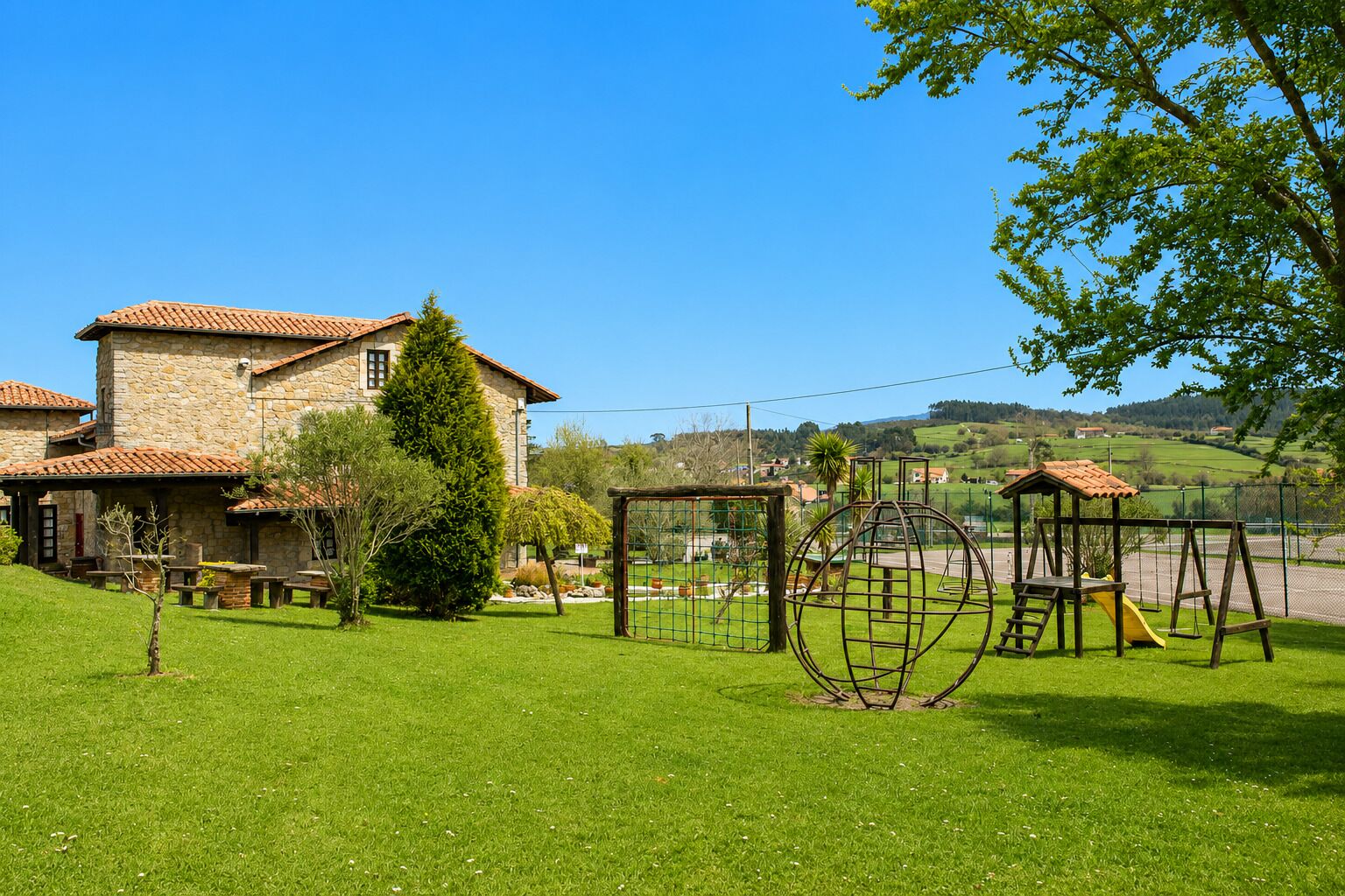 Uma casa de pedra com telhado de telhas vermelhas, um gramado e um parquinho com balanço e escorregador.