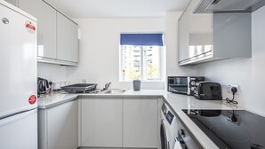 Cozinha compacta com armários brancos, forno embutido, micro-ondas e cafeteira.